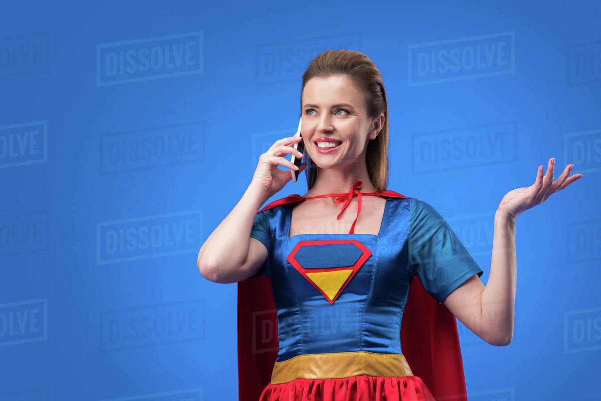 Portrait of smiling woman in superhero costume talking on smartphone ...