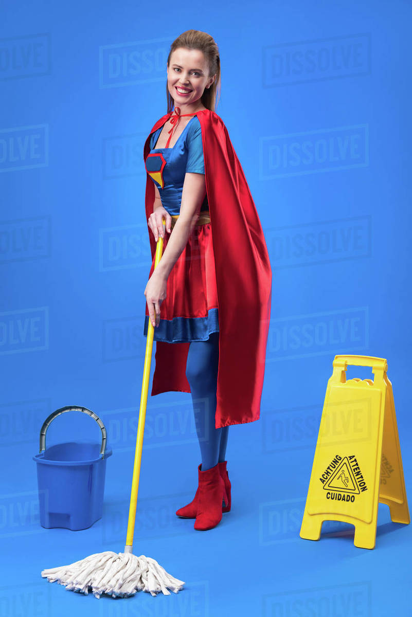 Smiling woman in superhero costume with caution sign, bucket and mop ...