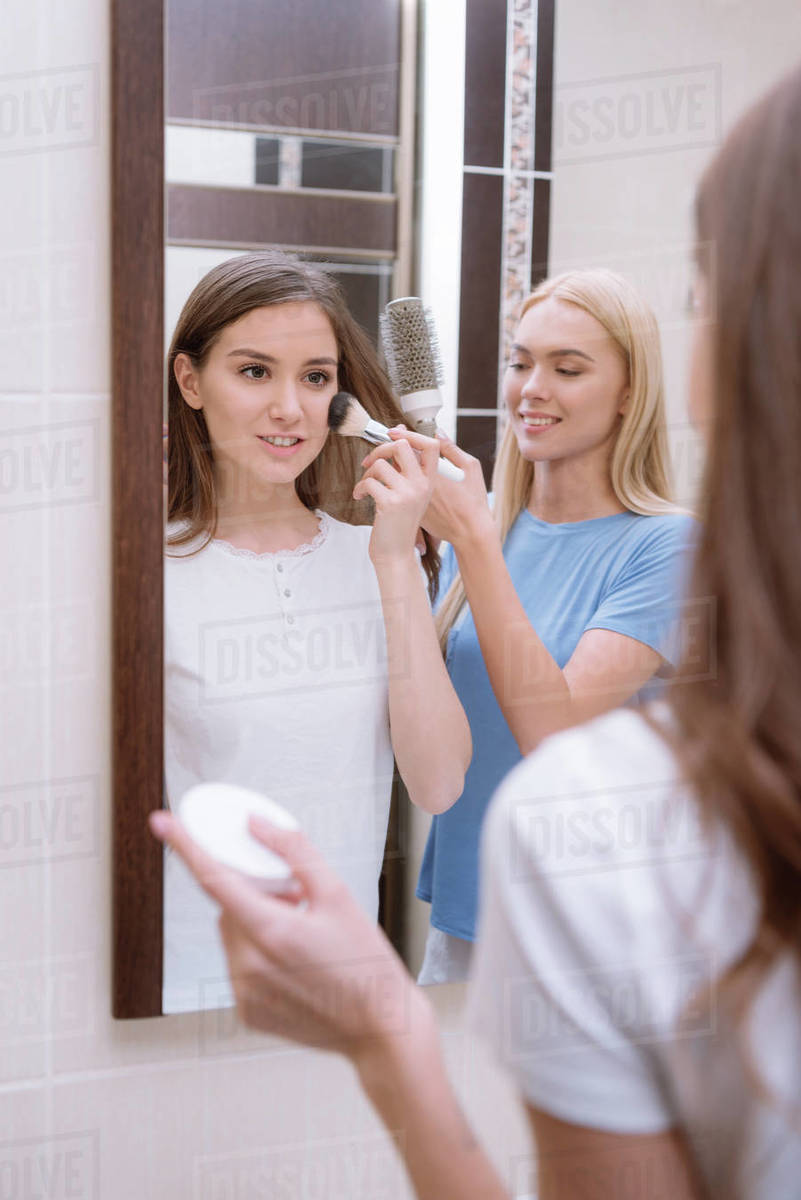 Girl applying foundation powder with makeup brush and friend combing ...