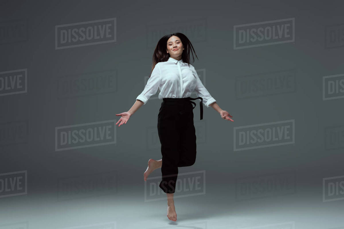 Happy barefoot girl jumping and smiling at camera on grey - Royalty ...