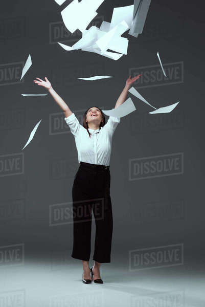 Full length view of happy young businesswoman throwing papers on grey ...