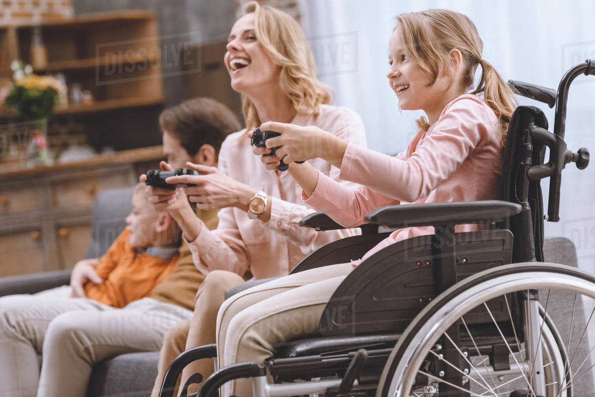 happy family with disabled child in wheelchair playing with joysticks ...