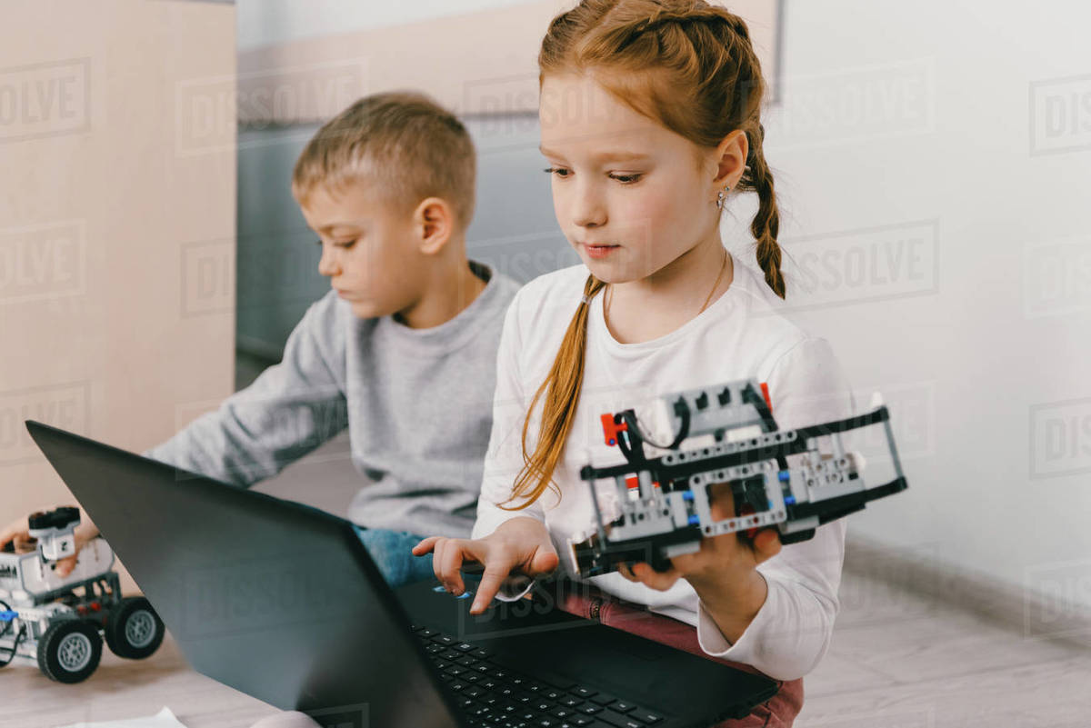 teen schoolgirl programming robot while sitting on floor with kid ...