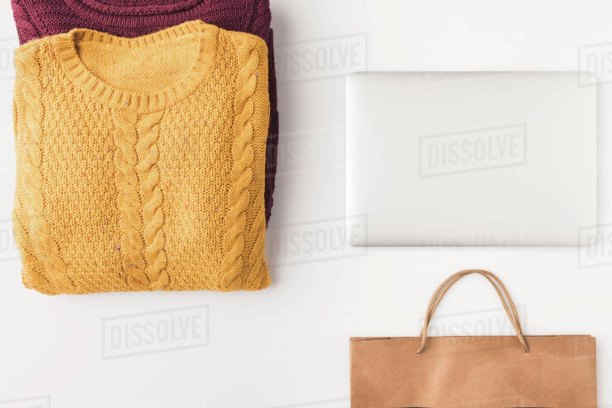 Flat lay with knitted sweaters, laptop and shopping bag, isolated on white - Stock Photo - Dissolve