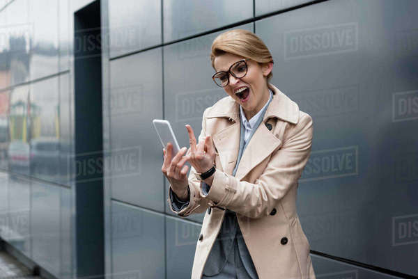 portrait of businesswoman with smartphone showing middle finger on ...