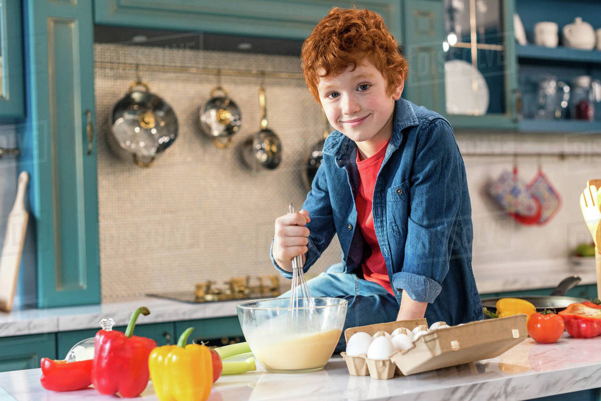 Cute little boy smiling at camera while cooking in kitchen - Royalty ...