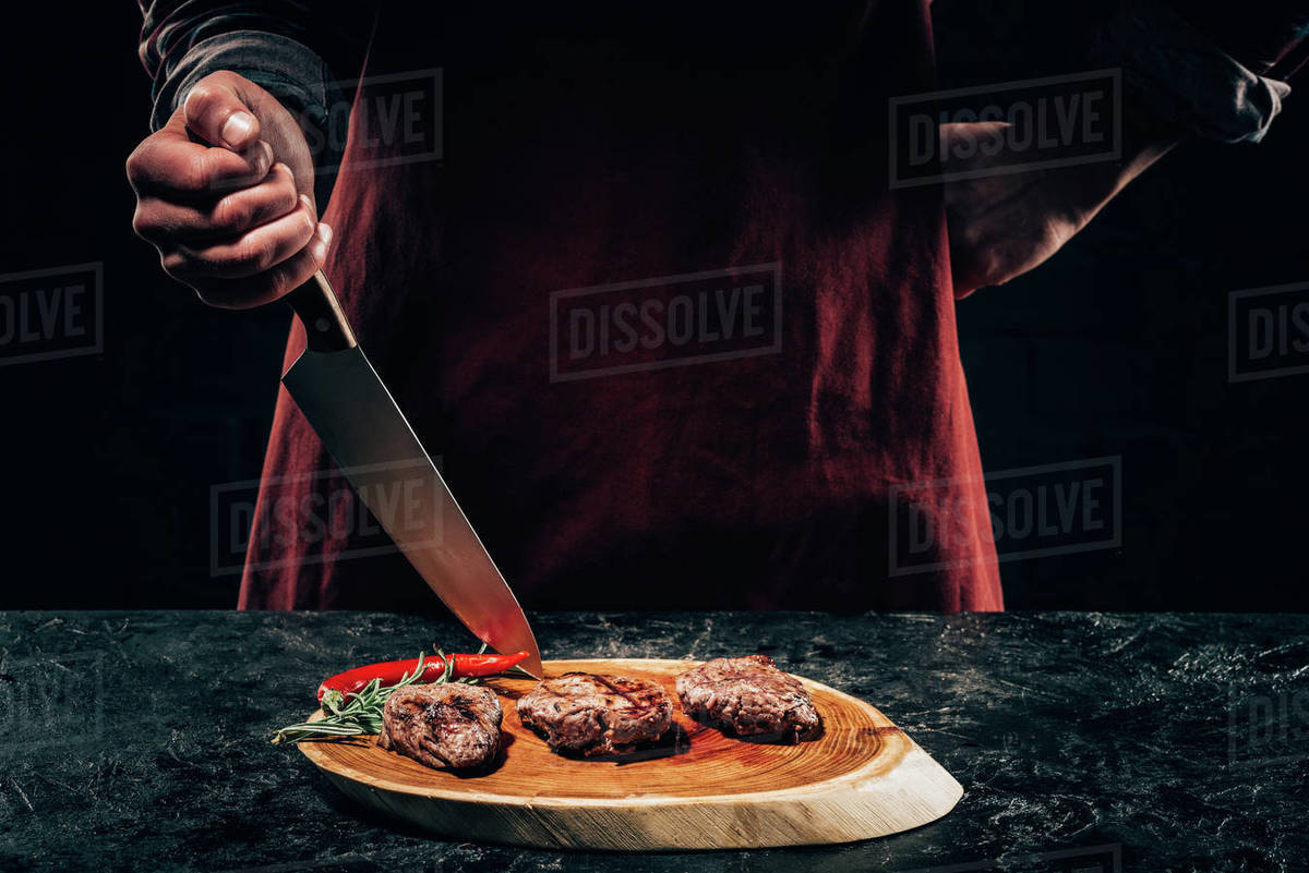 cropped shot of chef in apron standing with knife and delicious grilled ...