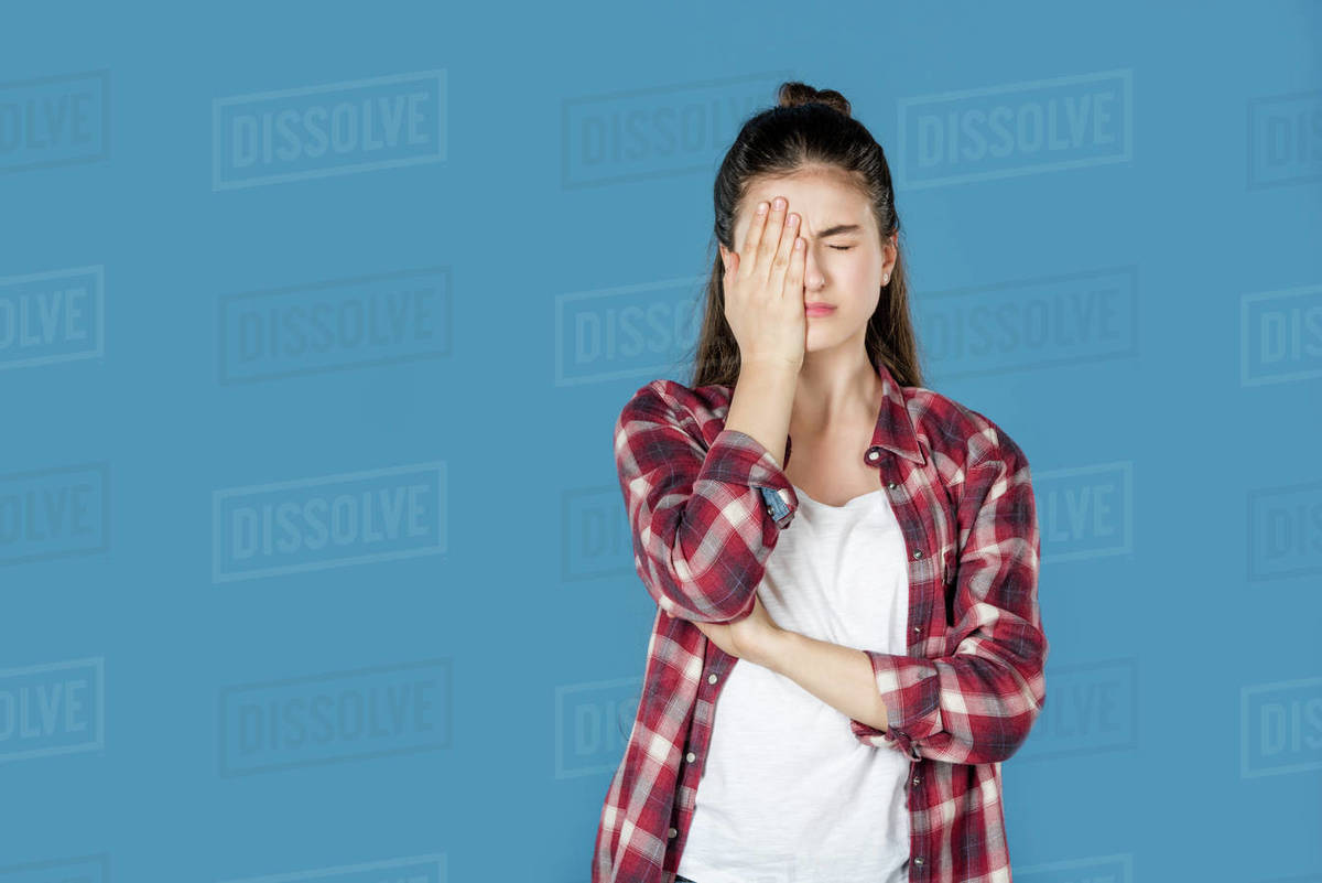 Ashamed teen girl covering half face with hand isolated on blue ...