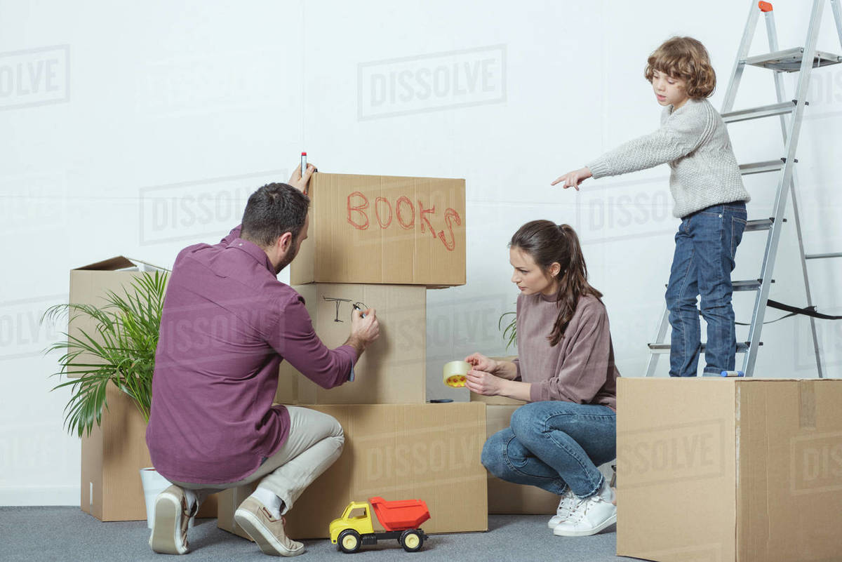 Parents packing boxes and son pointing with finger during relocation ...