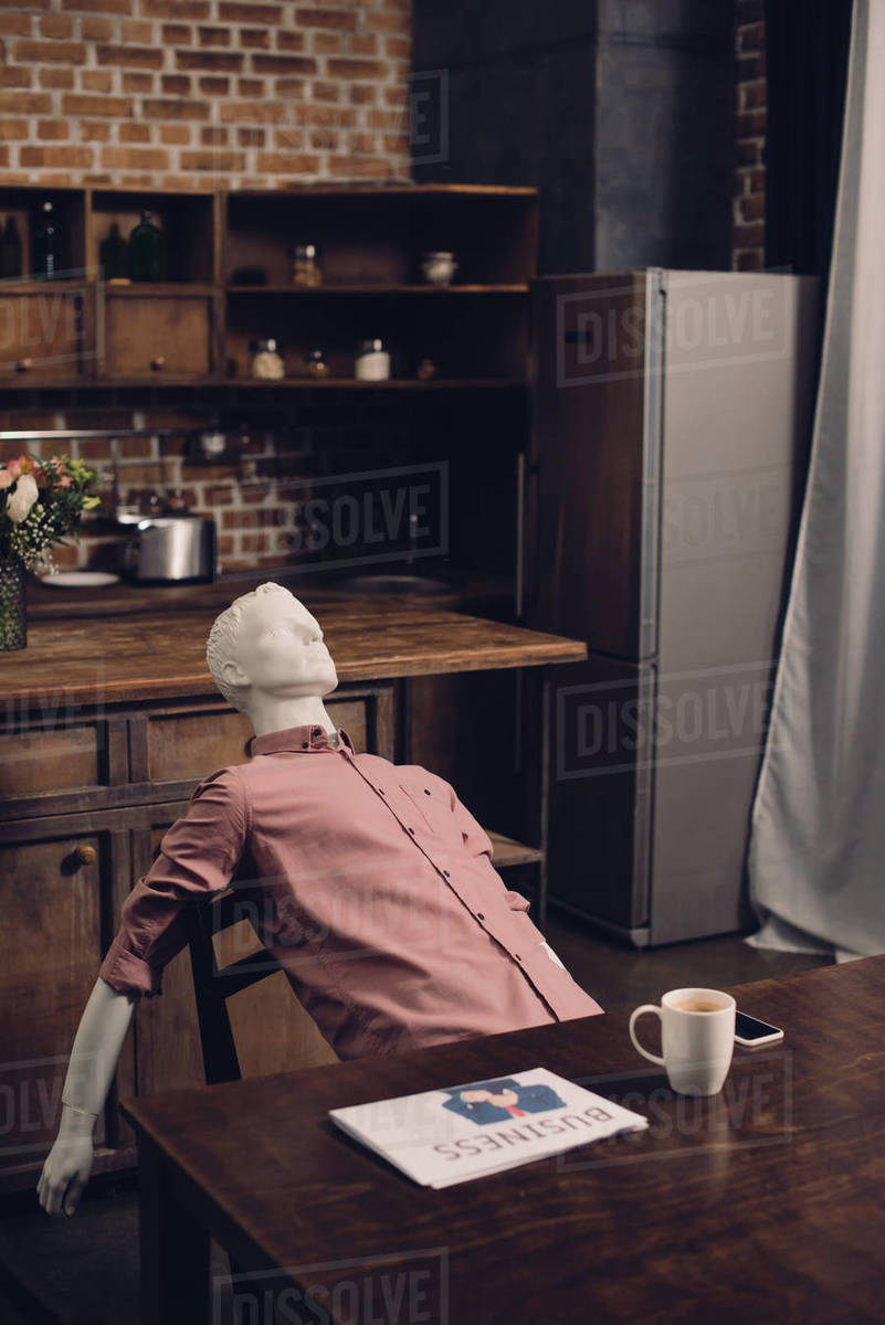 Close up view of manikin at table with cup of coffee and newspaper in ...