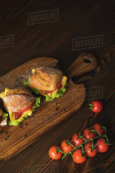 Overhead view of cheese sandwiches on wooden board and cherry tomatoes ...