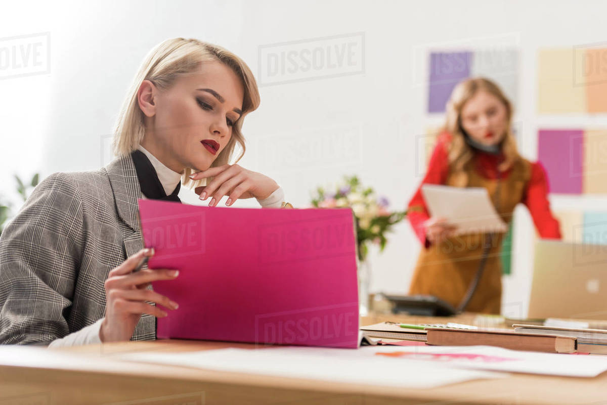Fashion magazine editor doing paperwork in modern office with colleague ...