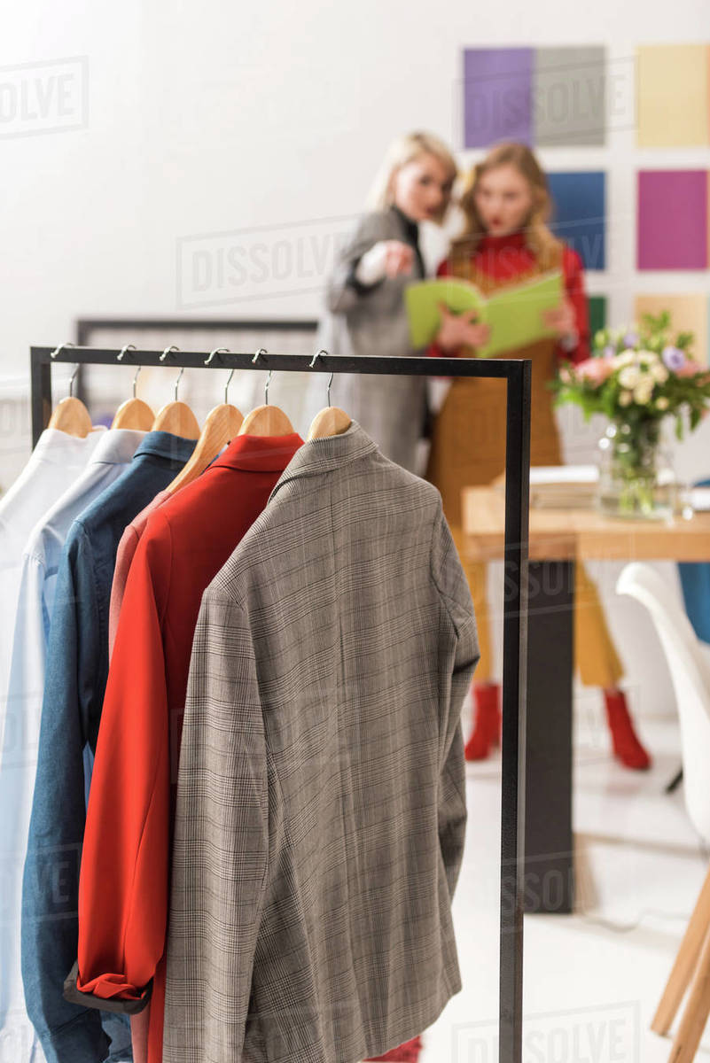Stylish dressmakers working in modern office with clothes on foreground ...
