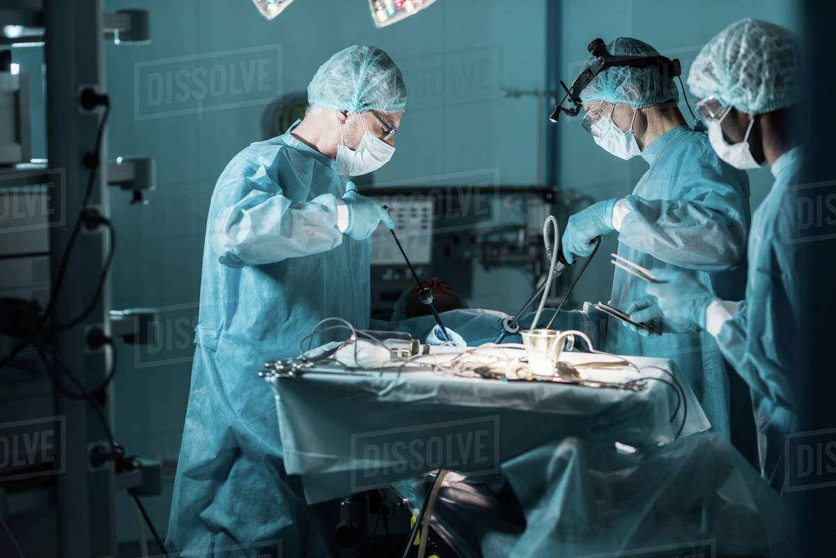 Side view of multiethnic surgeons operating patient in operating room ...