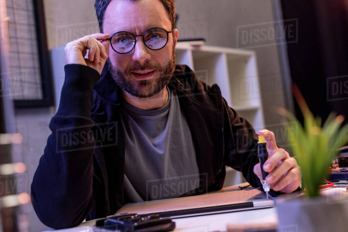 Man with hand on glasses using screwdriver while fixing digital tablet ...