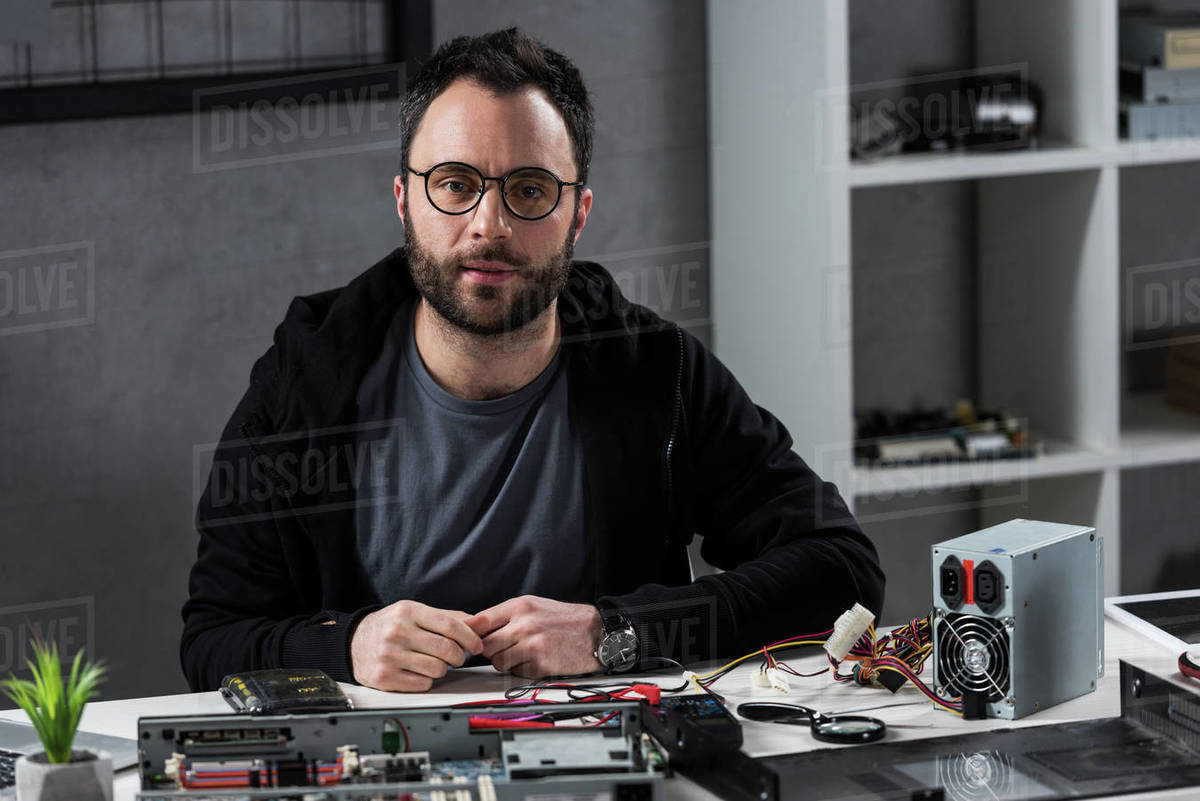 Man sitting against broken computer on table and looking at camera ...