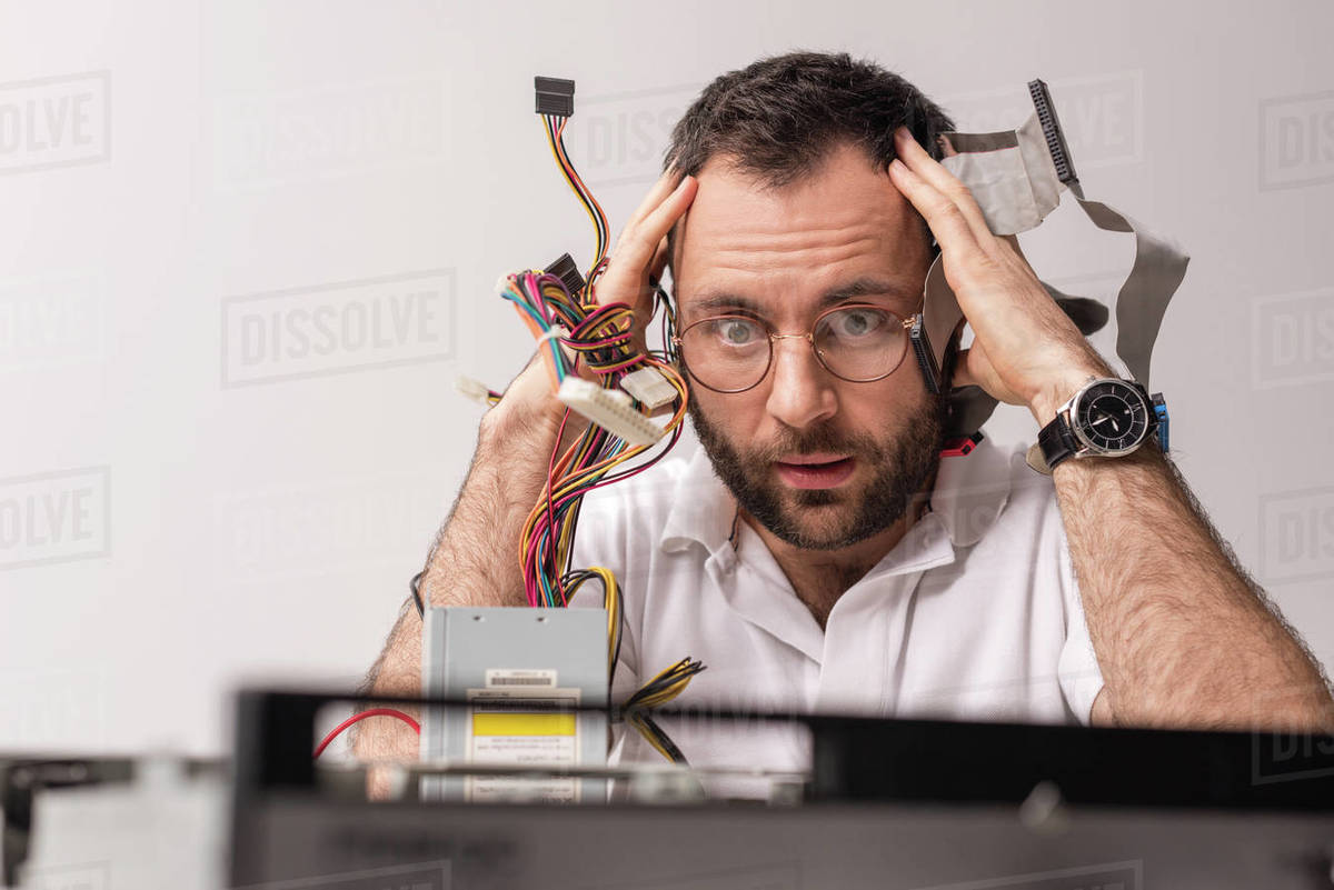 Scared man with wires in hands near his head looking on broken pc ...