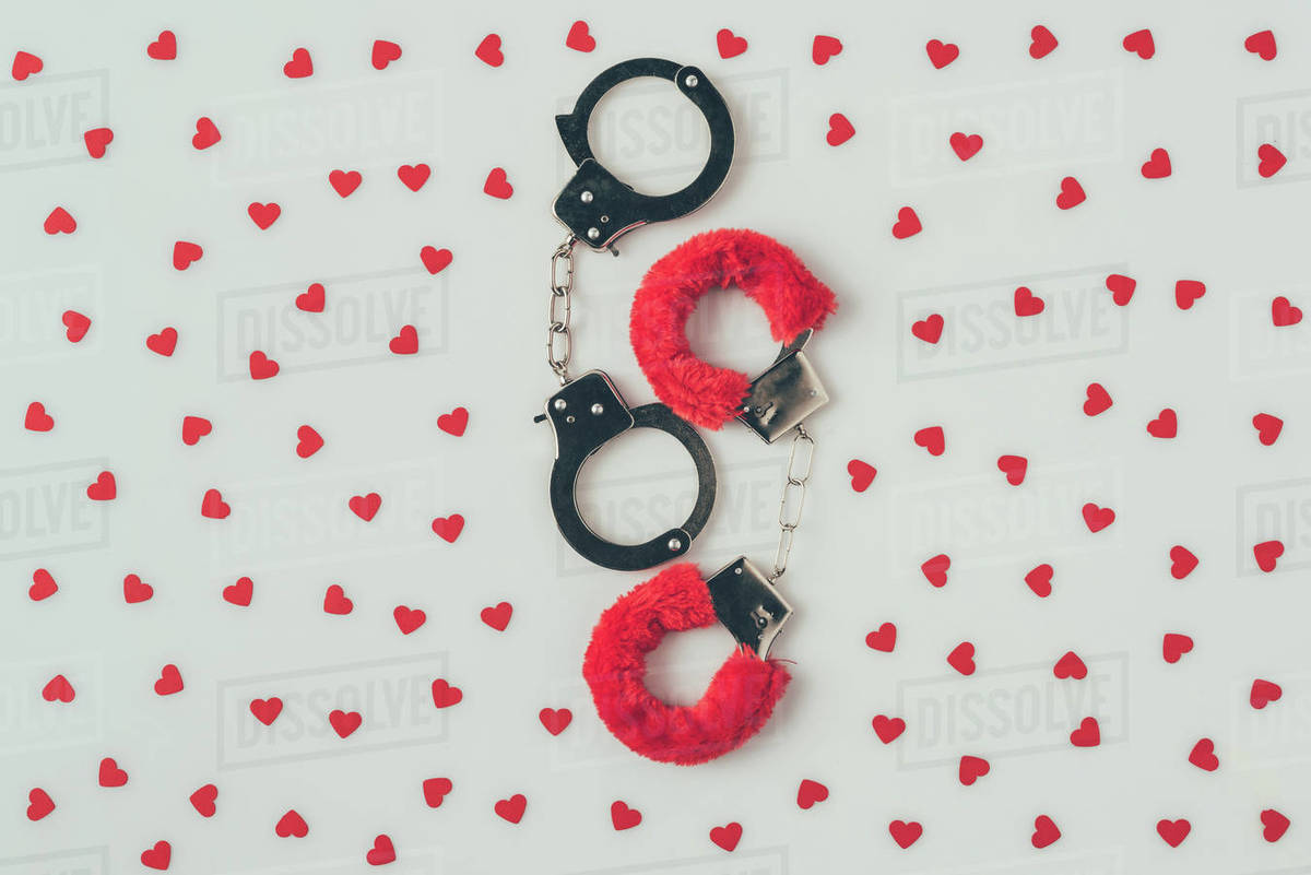Top view of black and red handcuffs with scattered paper hearts ...