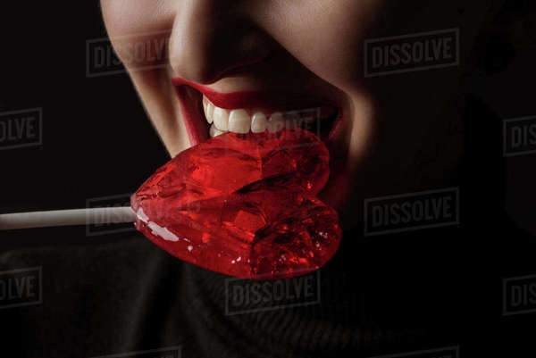 Cropped image of woman biting heart shaped lollipop isolated on black ...