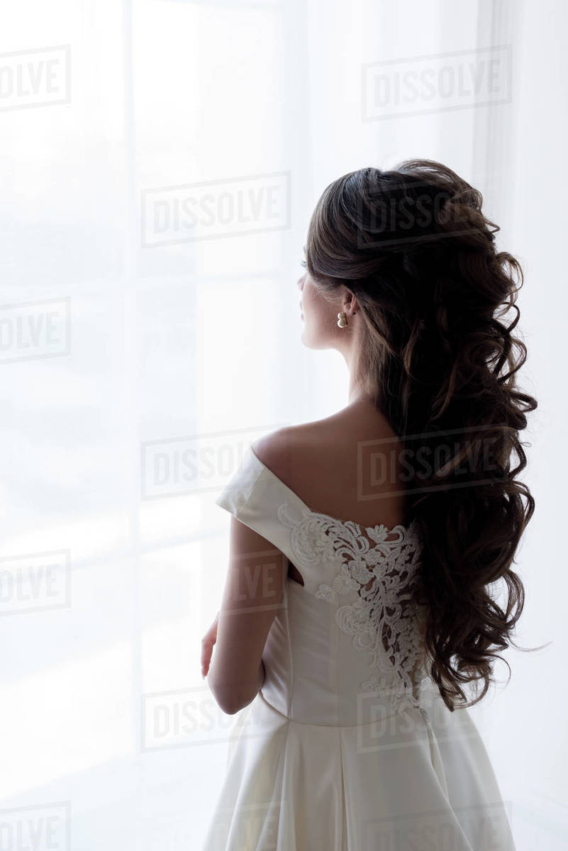 Back view of bride in wedding dress looking at window - Royalty-free ...