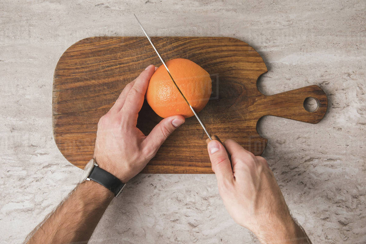 Cropped image of man cutting orange - Stock Photo - Dissolve