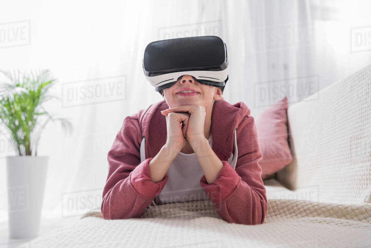 Girl lying on sofa and watching something with virtual reality headset ...