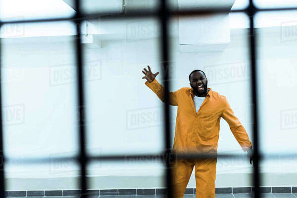 African American prisoner screaming in prison cell - Stock Photo - Dissolve