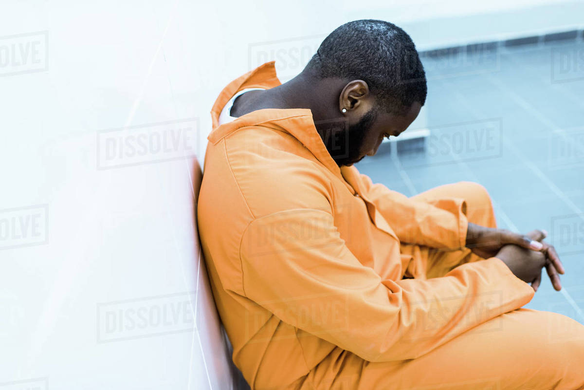 Sad African American prisoner sitting on bench in prison cell - Royalty ...