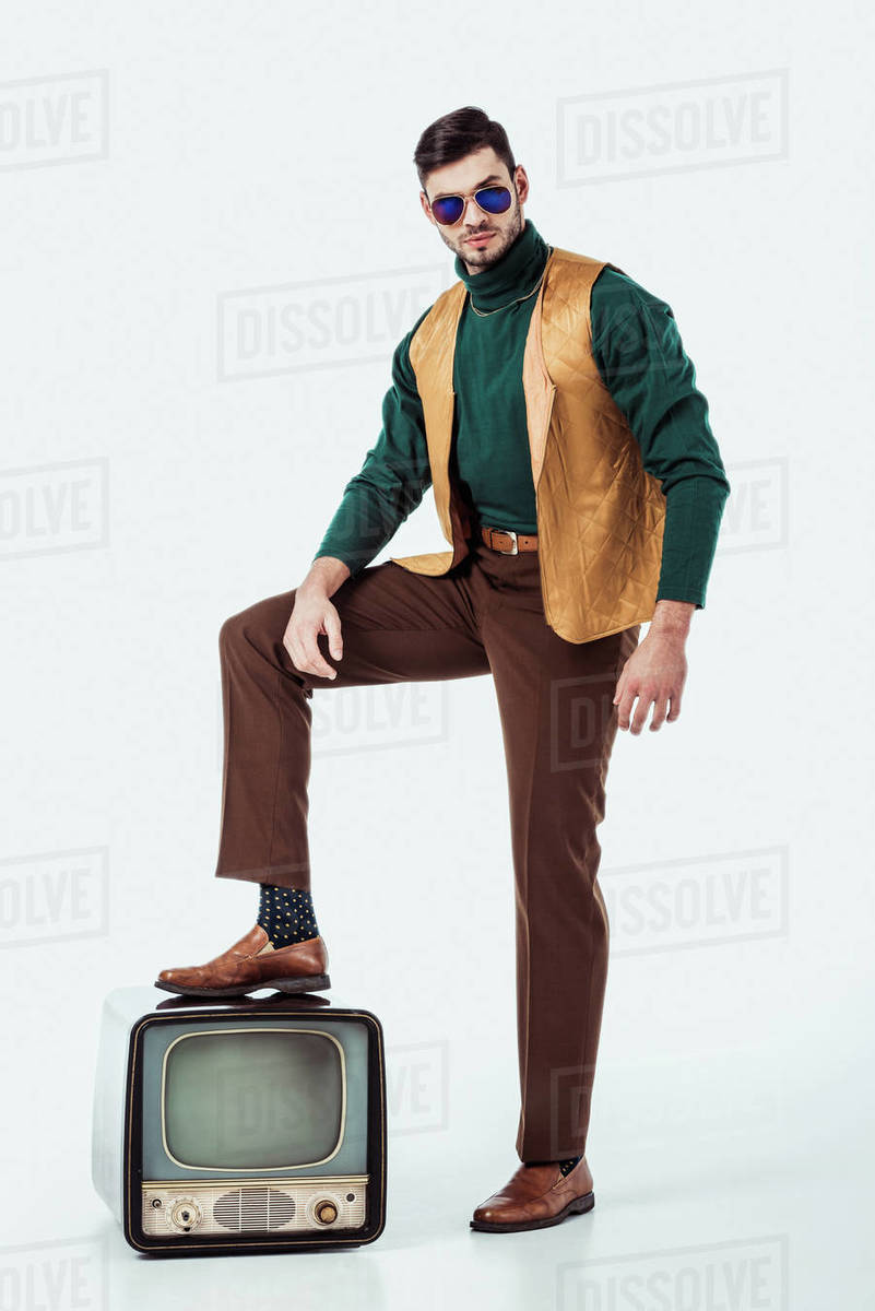 Handsome retro styled man putting leg on vintage television on white ...