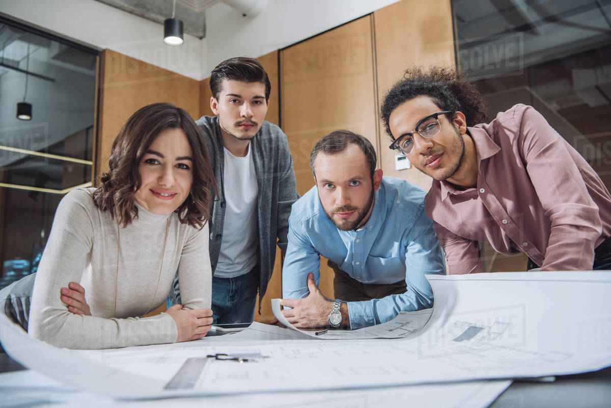 Group of successful architects working on plans together at office ...