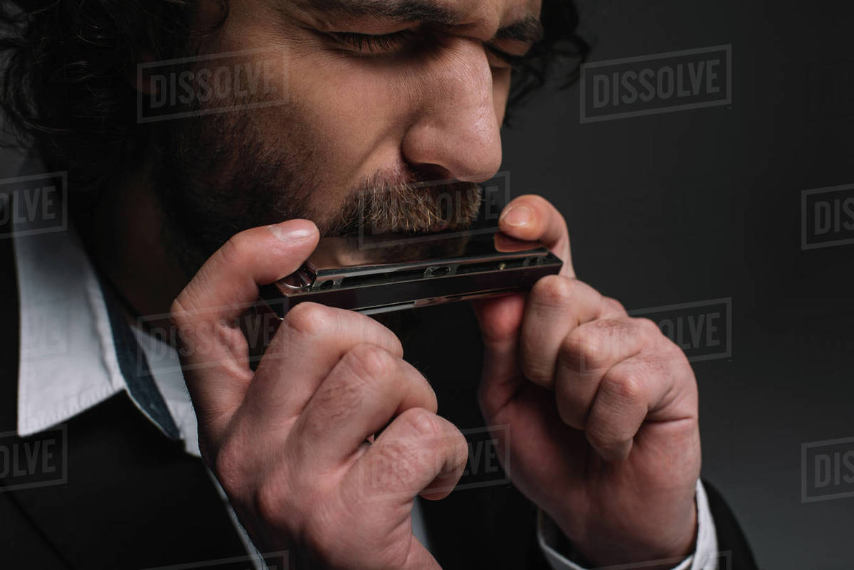 Close-up portrait of expressive musician playing harmonica on black ...