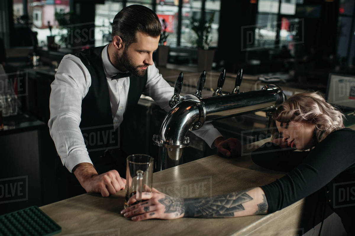 Bartender looking at drunk girl sleeping at bar counter - Royalty-free ...
