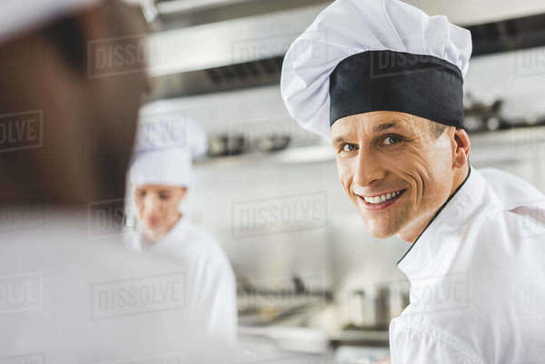 Handsome smiling chef looking at camera at restaurant kitchen - Royalty ...