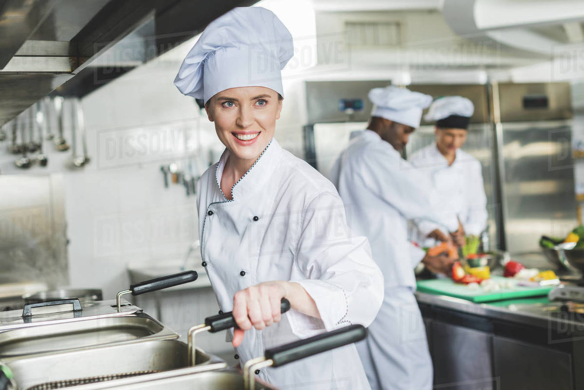 Attractive chef frying food in oil at restaurant kitchen and looking ...