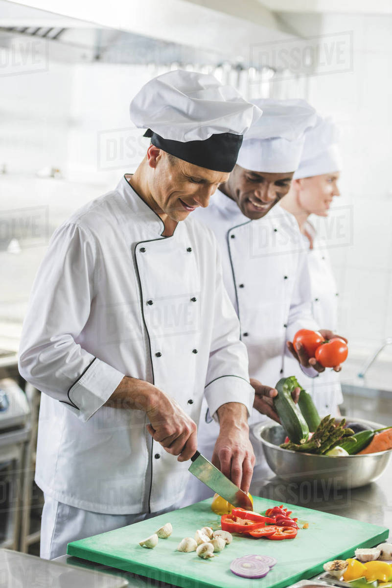 Smiling multicultural chefs preparing food at restaurant kitchen ...