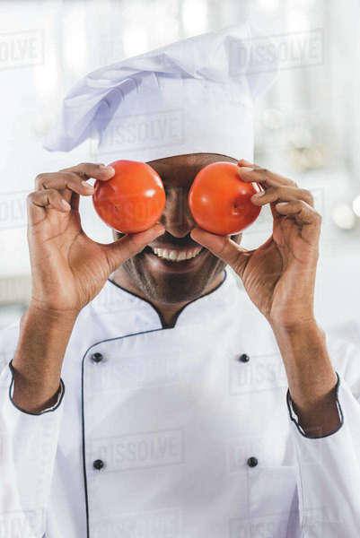 Handsome African American chef covering eyes with tomatoes at ...