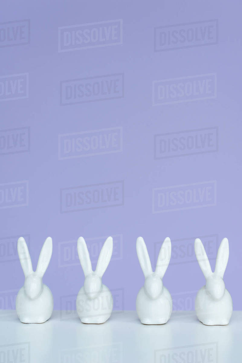 Bunny statuettes in row on violet background - Stock Photo - Dissolve