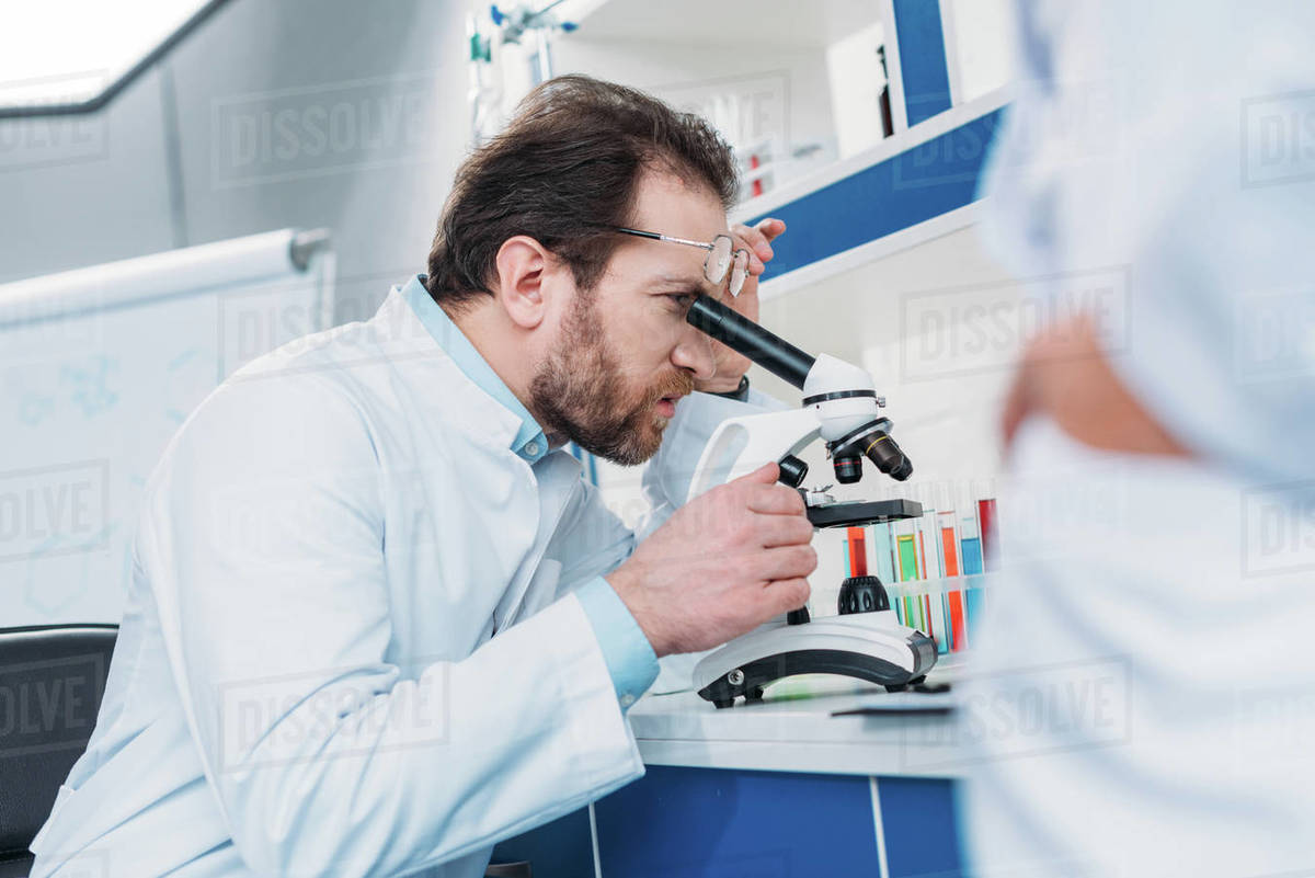 scientist in lab coat looking through microscope on reagent with ...