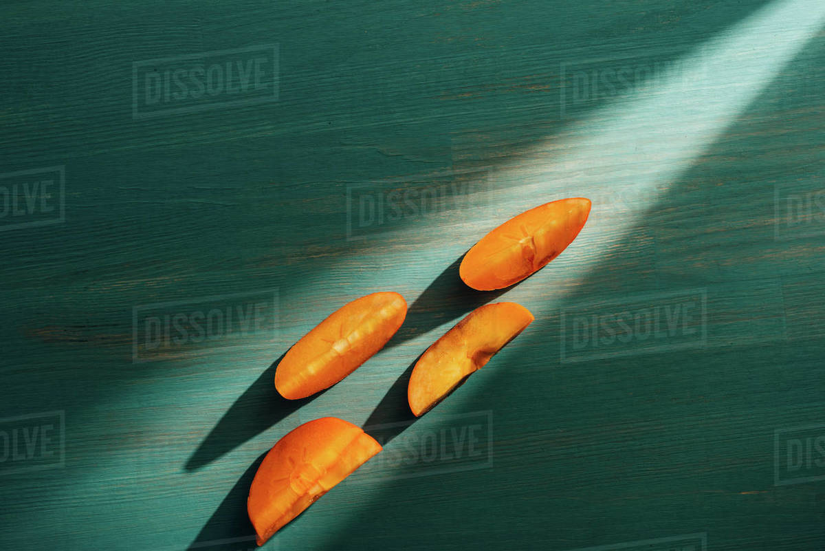 top view of persimmon persimmon pieces on table with light and shadow ...
