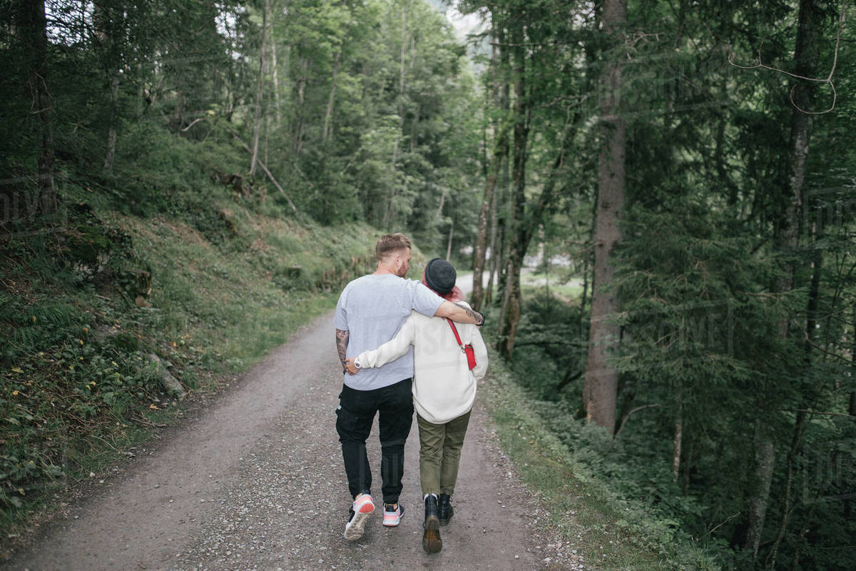 back view of young couple embracing and walking on pathway in green ...