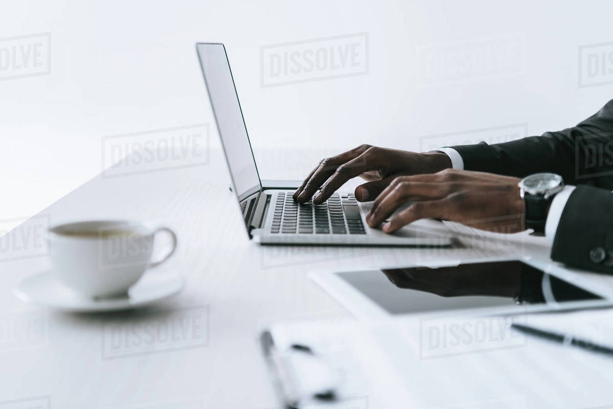 partial view of african american businessman typing on laptop at ...