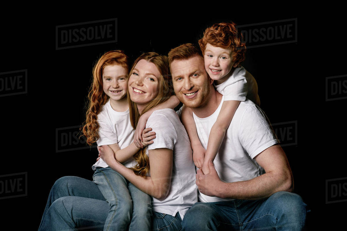 Happy redhead family sitting embracing and smiling at camera isolated ...