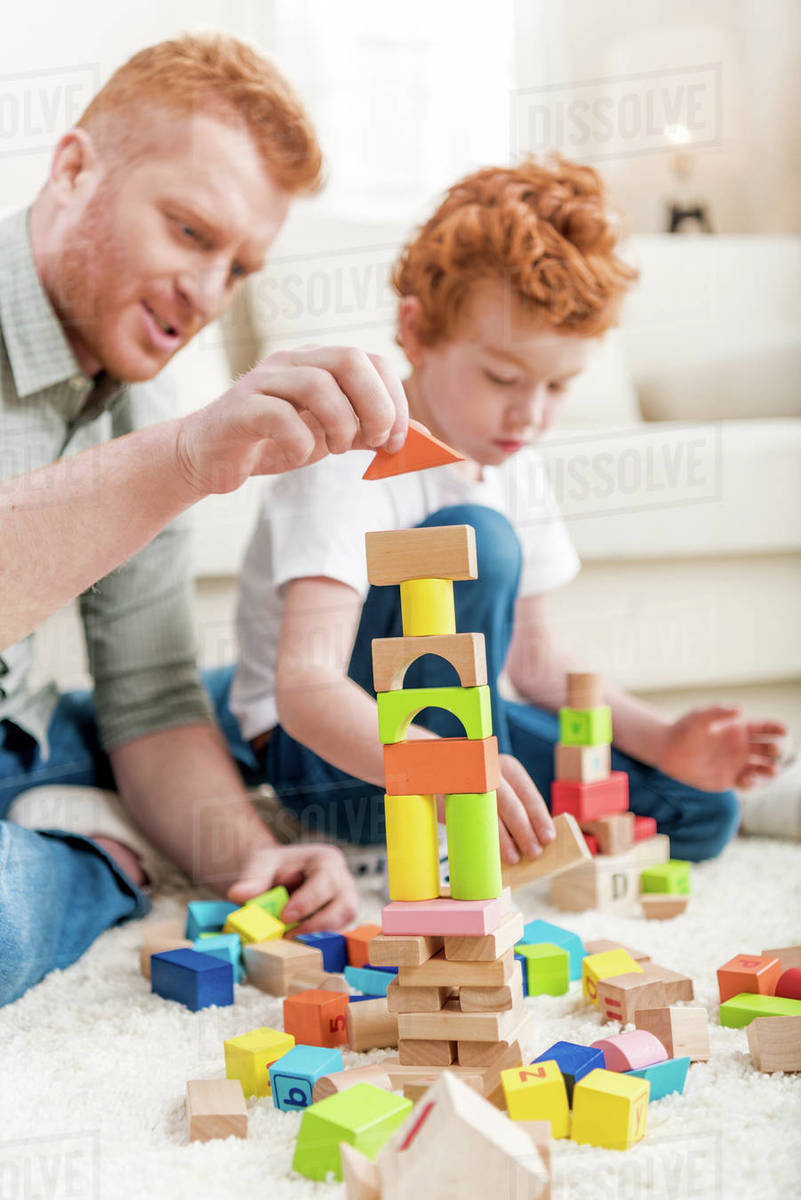 father and adorable son playing with constructor on floor at home ...