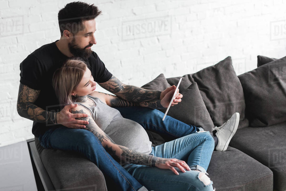 Pregnant girlfriend looking at tablet with boyfriend at living room ...