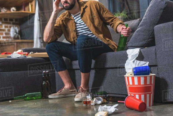 Cropped image of loner holding bottle of alcohol drink at living room ...