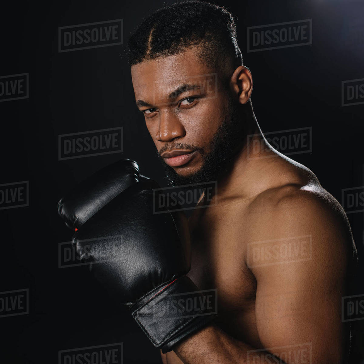 Serious shirtless African American boxer in boxing gloves looking at ...