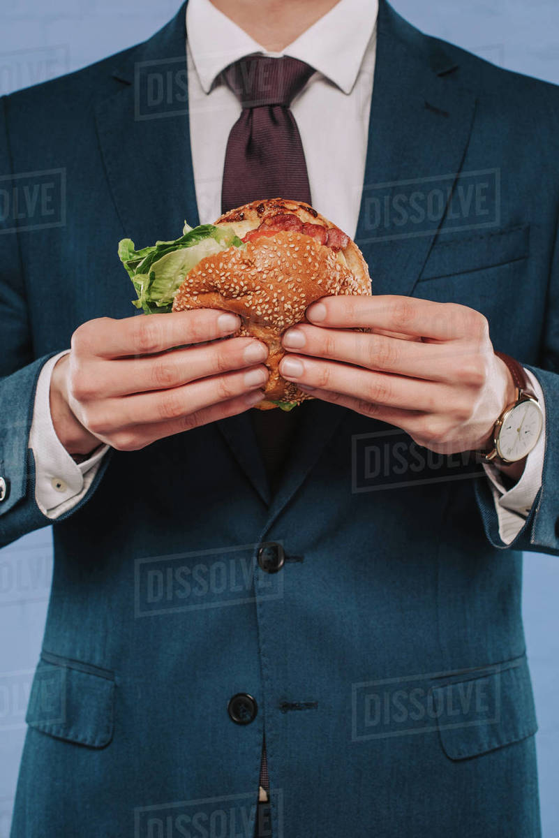 Cropped shot of businessman in formal suit holding burger - Royalty ...