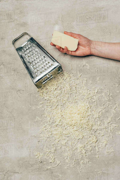 Close-up view of hand holding cheese by grater on light background ...