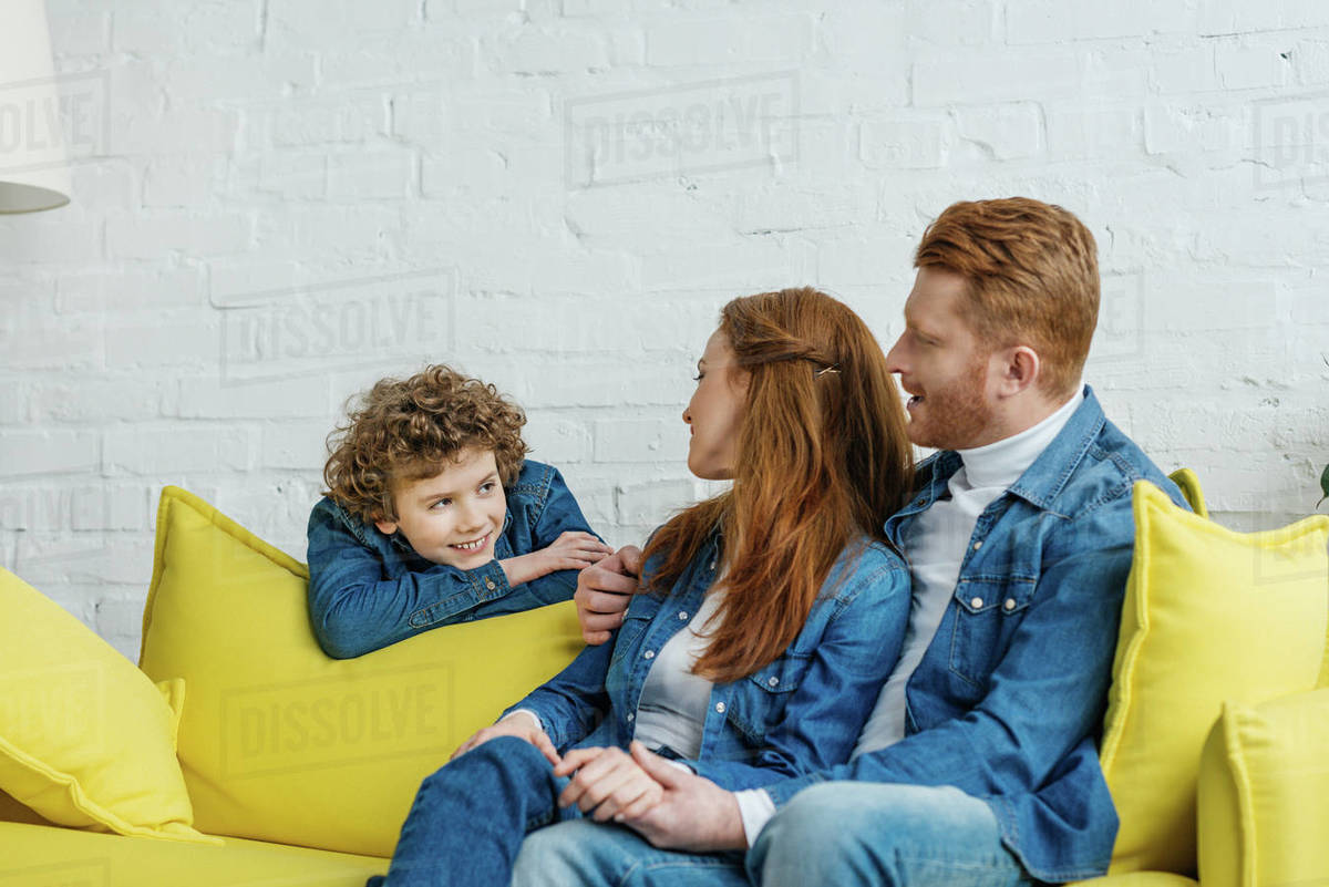 Parents sitting on sofa and looking at smiling son - Royalty-free Stock ...