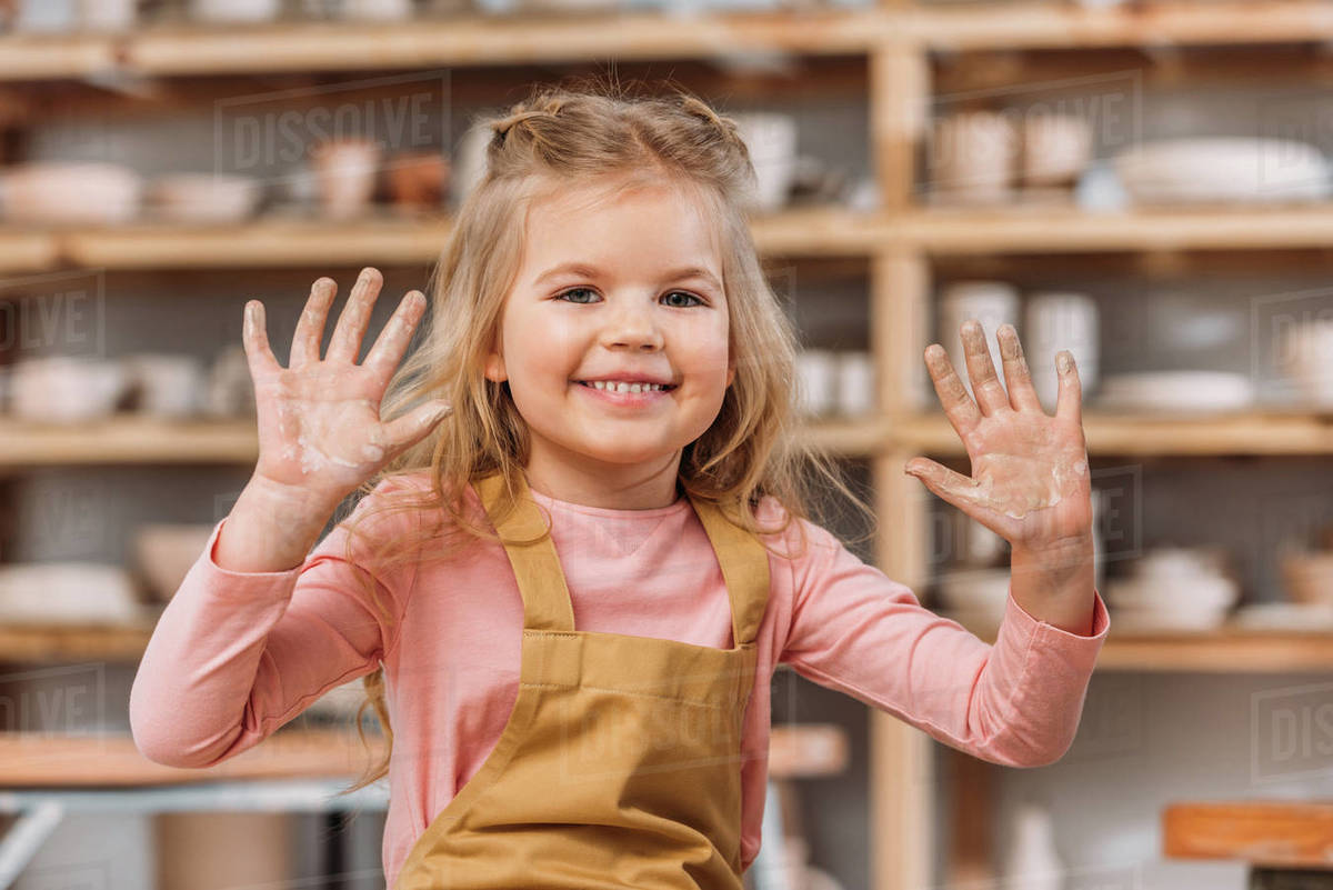 Adorable smiling child showing hands in clay - Stock Photo - Dissolve